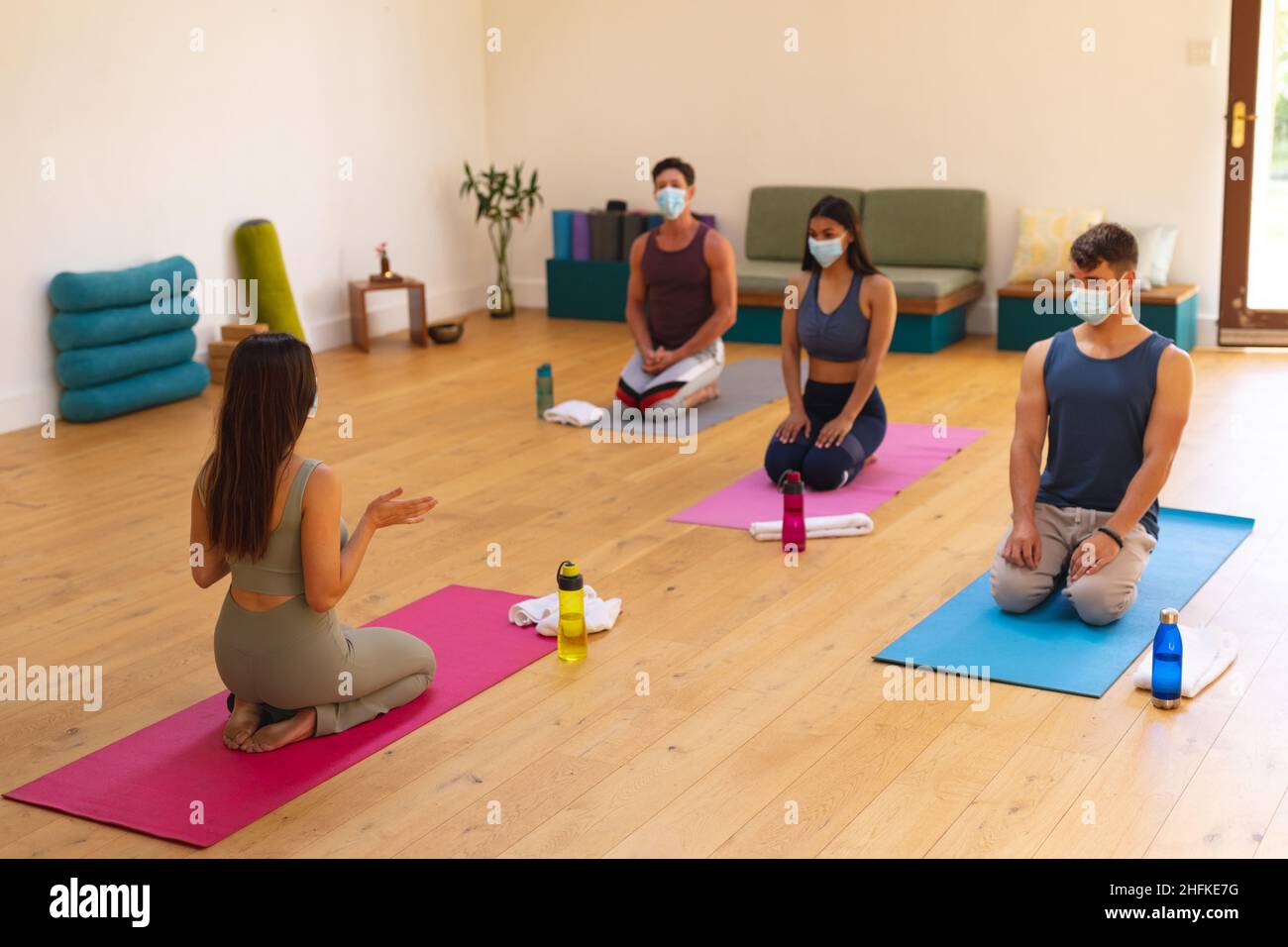 Female instructor with multiracial men and women wearing face masks in yoga studio during covid ...