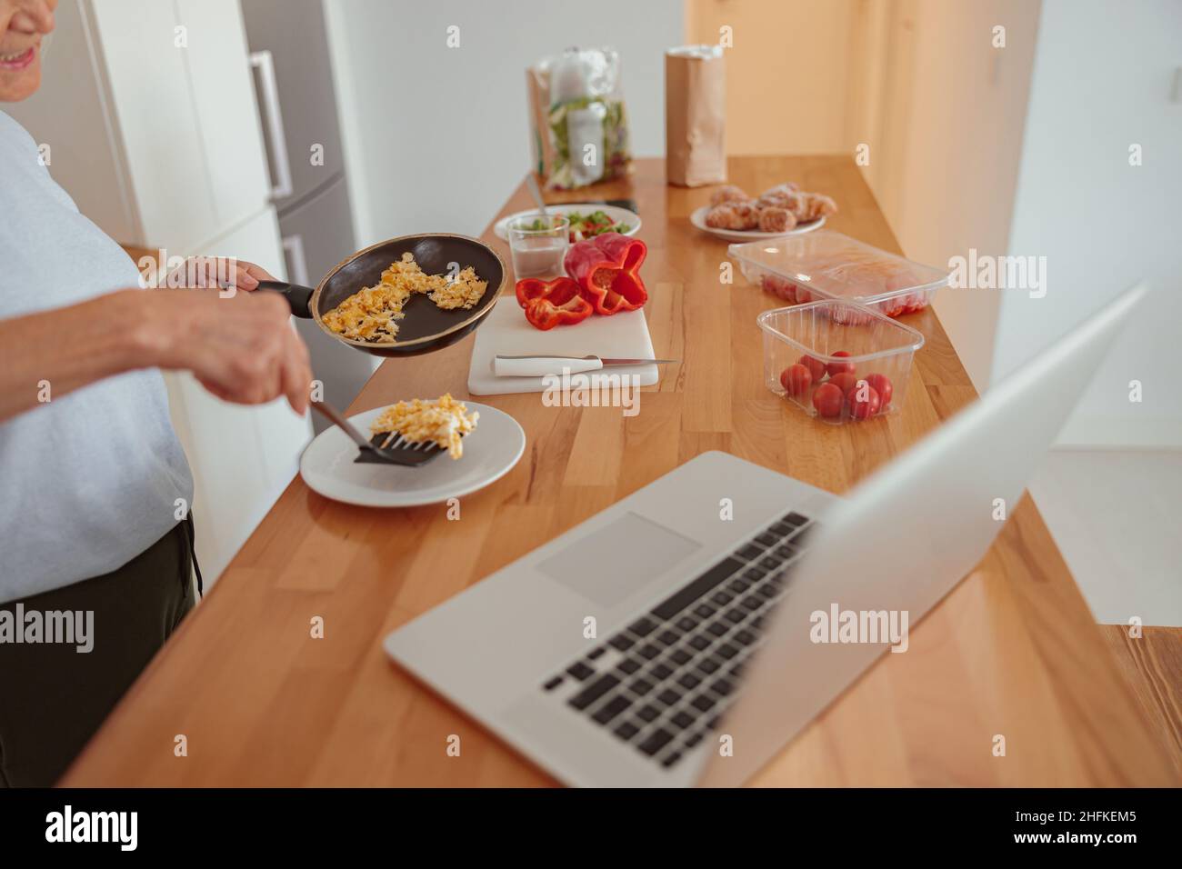 Pensioner female using laptop while cooking at kitchen Stock Photo - Alamy