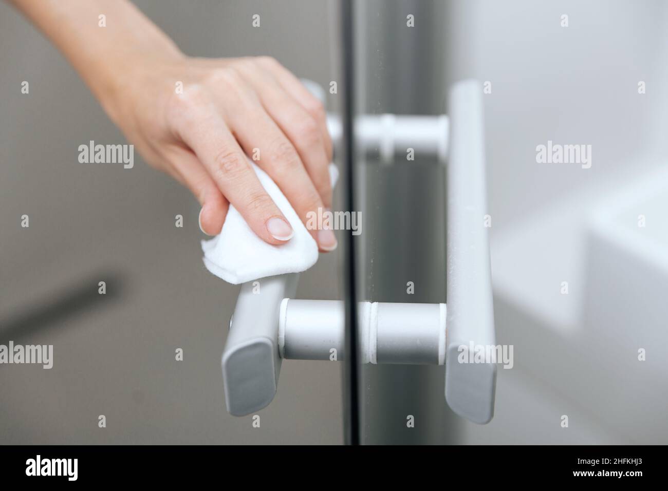 Cleaning glass door handles with an antiseptic wet wipe. Woman hand ...