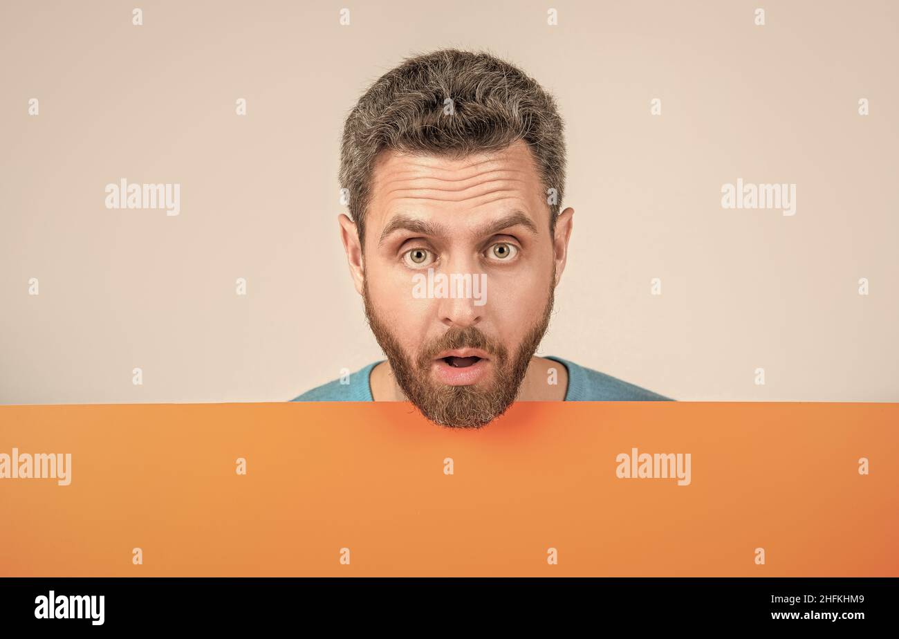 surprised mature bearded man behind orange black paper banner with copy ...