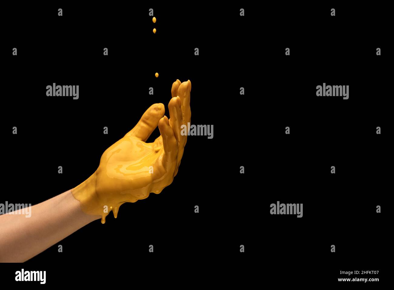 Yellow painted human hand gesturing isolated on dark studio background ...