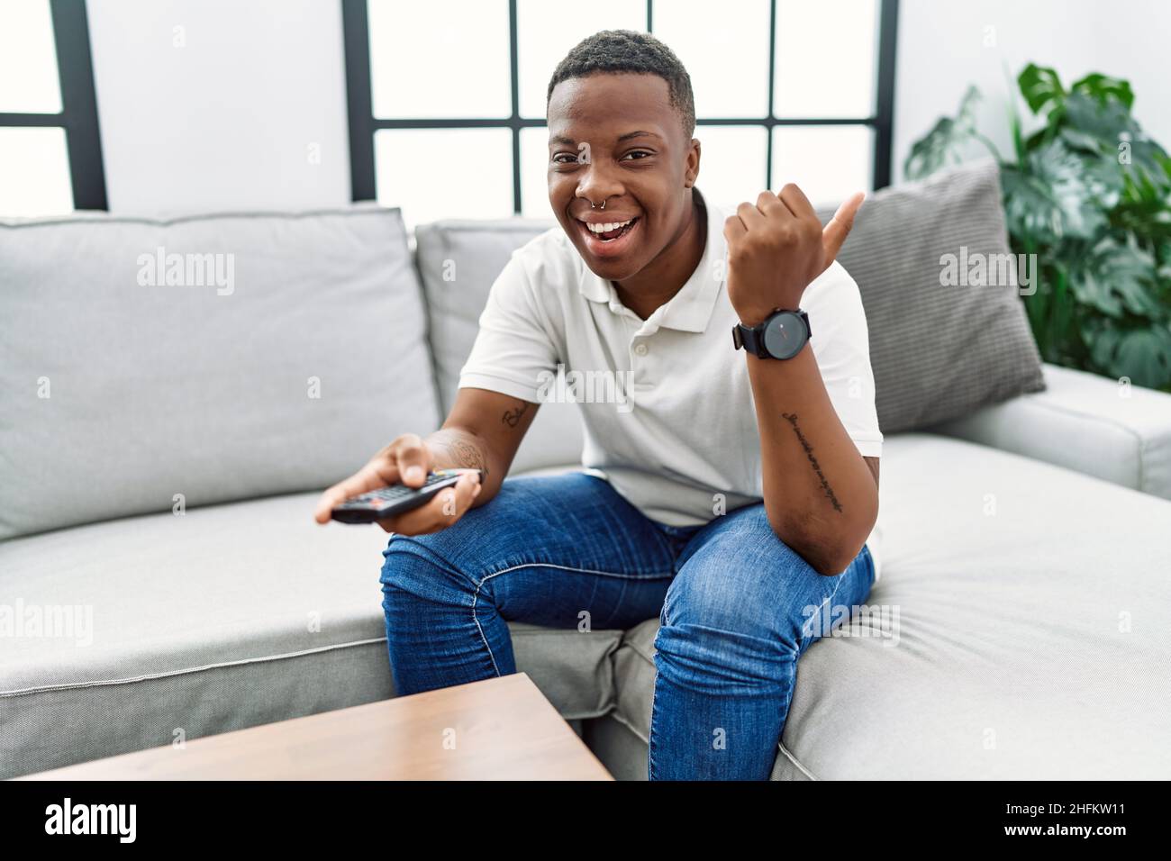 Young african man watching tv holding television remote control ...
