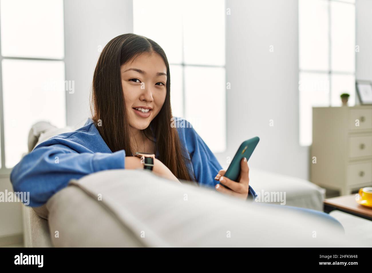 Young chinese girl using smartphone sitting on the sofa at home Stock ...