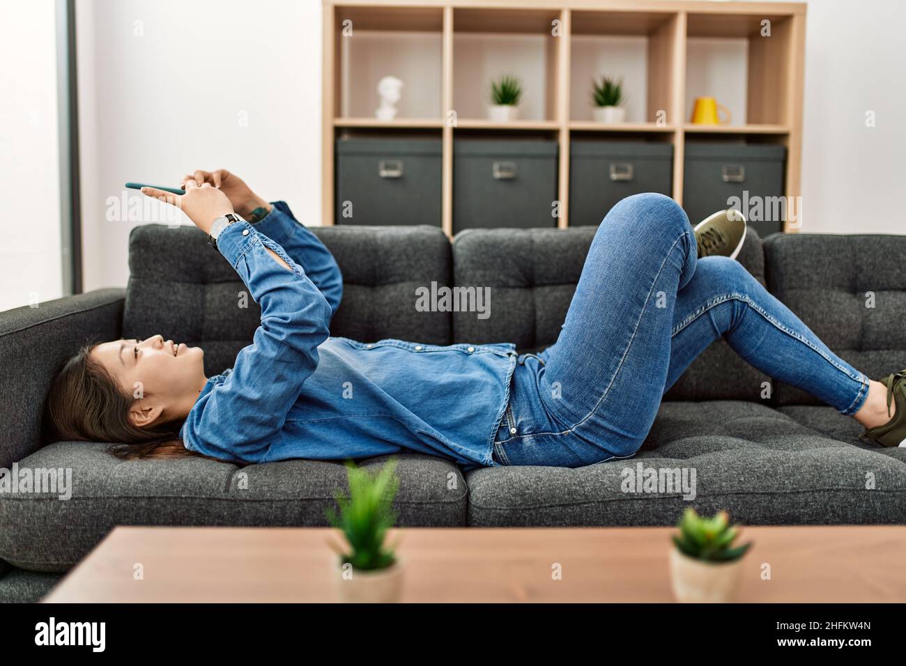 Young chinese girl using smartphone lying on the sofa at home Stock ...