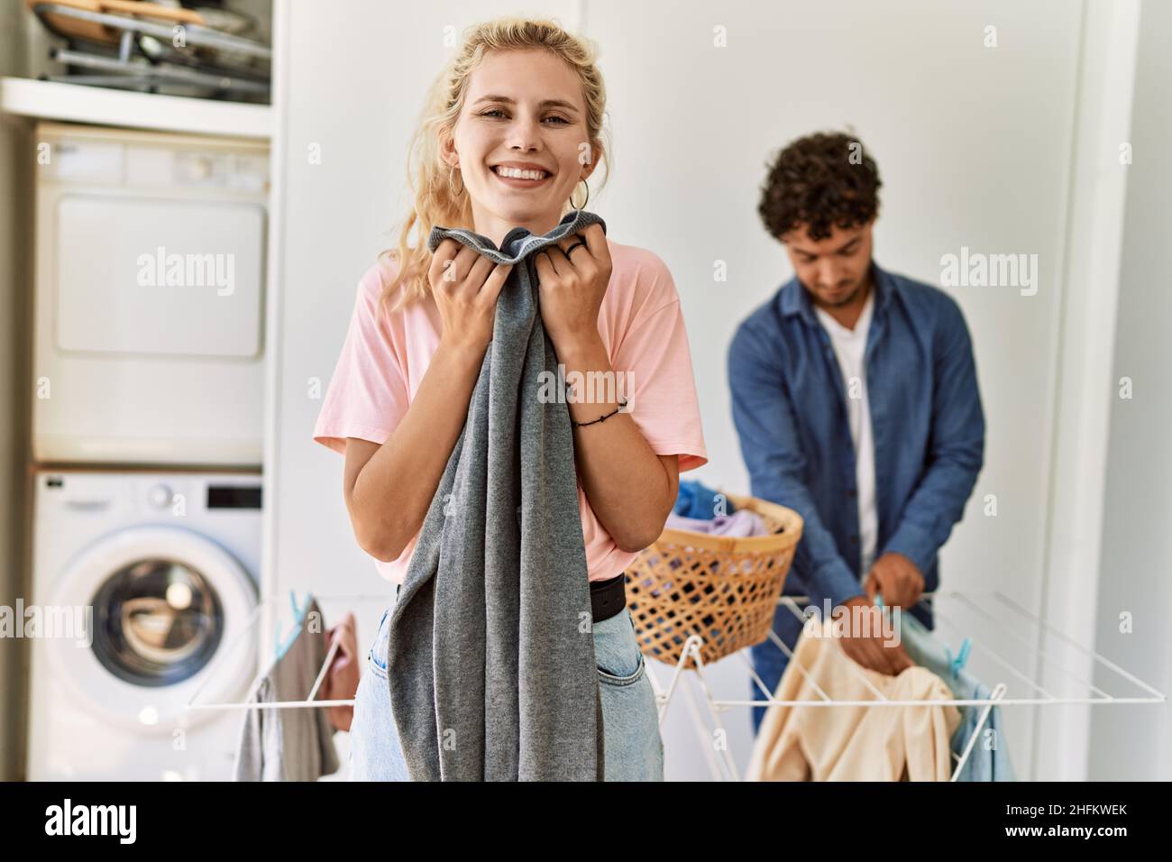 Young couple smiling happy doing laundry. Woman smelling clean clothes ...
