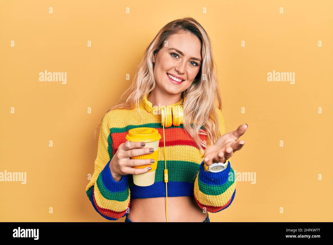 Beautiful young blonde woman drinking cup of coffee wearing headphones ...