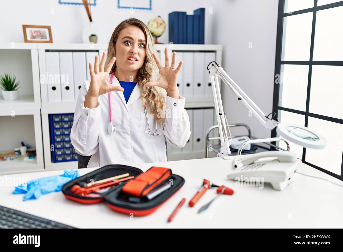 Young beautiful doctor woman with reflex hammer and medical instruments ...