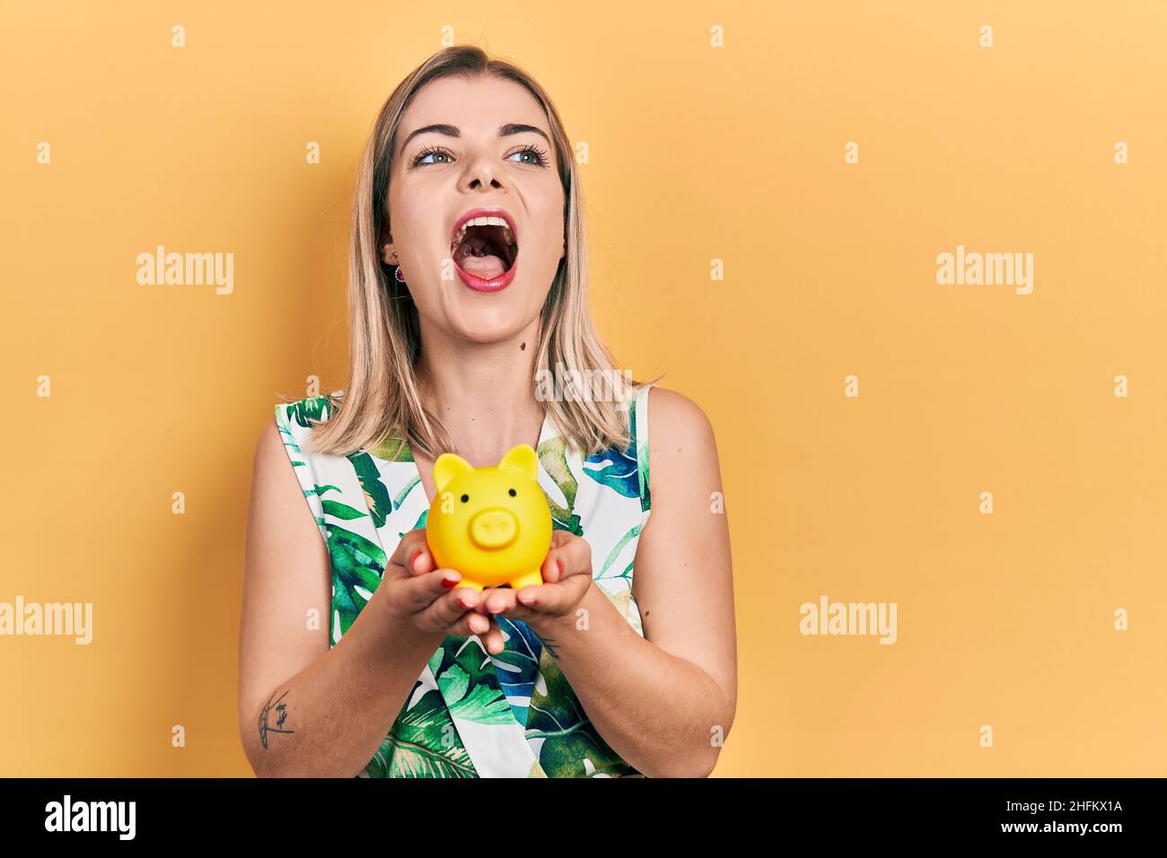 Beautiful caucasian woman holding piggy bank angry and mad screaming ...