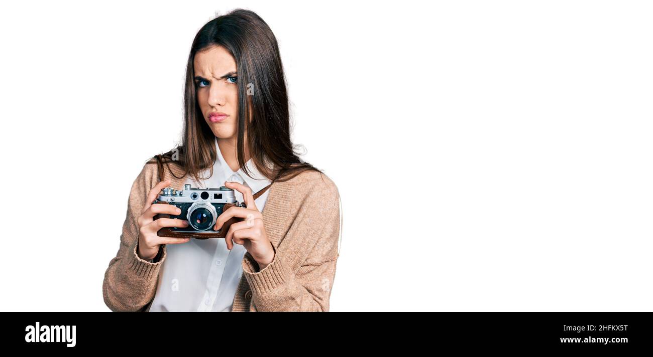 Young brunette teenager holding vintage camera clueless and confused ...