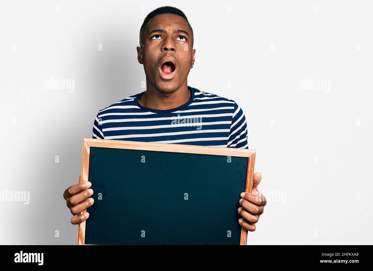 Young african american man holding blackboard angry and mad screaming ...