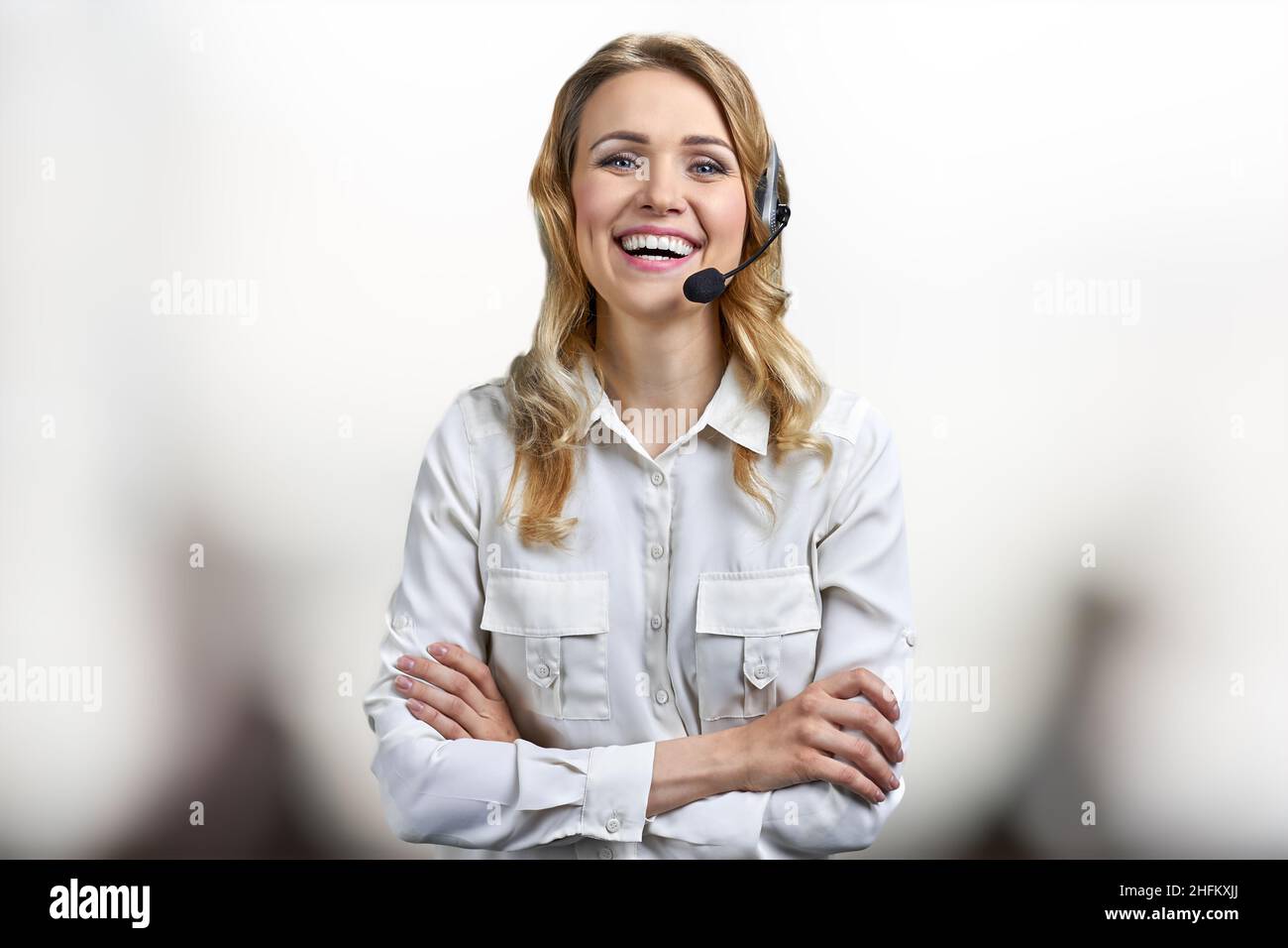 Happy call center operator with headset crossing arms on blurred ...