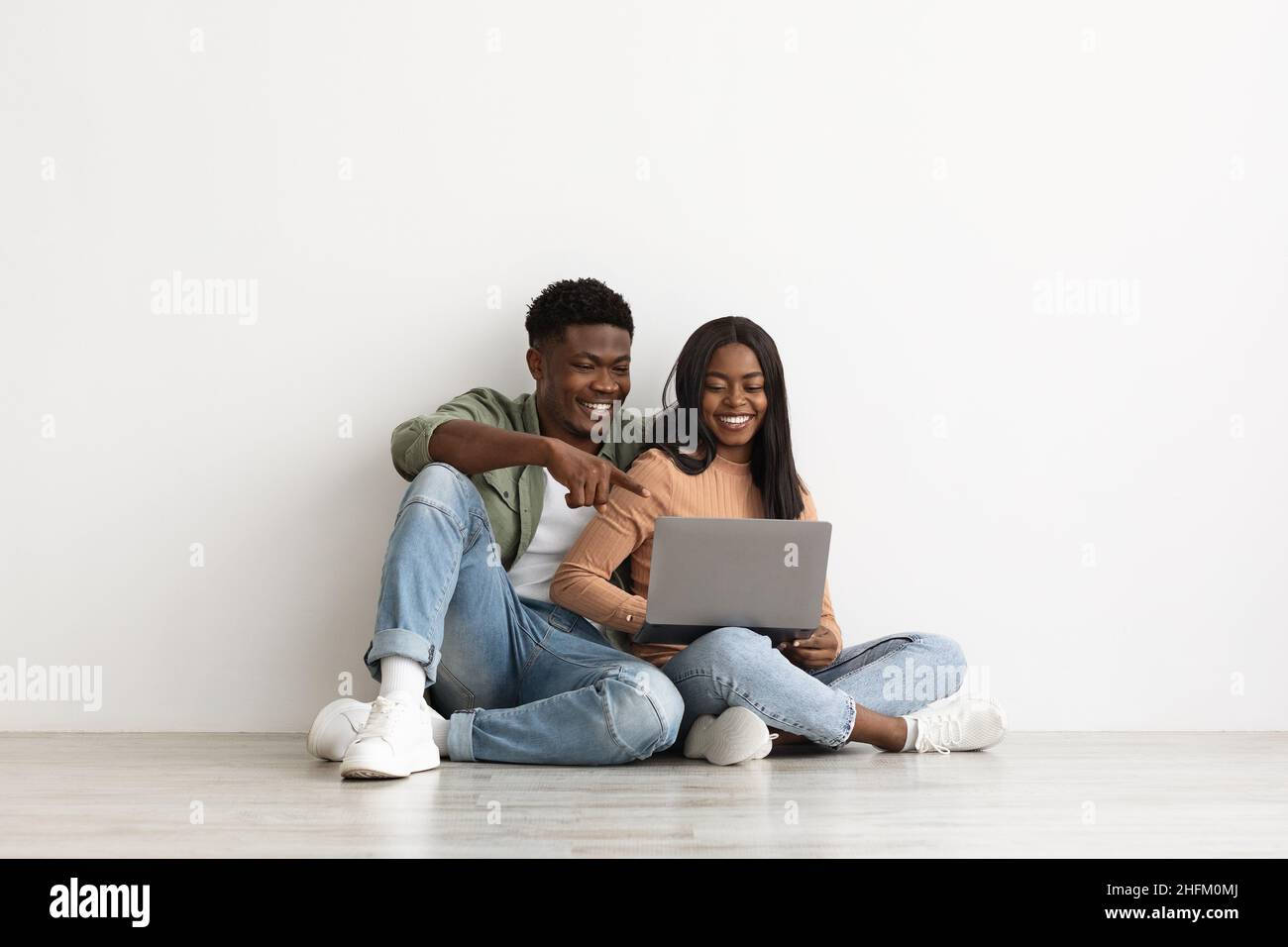 Happy black couple sitting on floor with laptop, having conversation ...