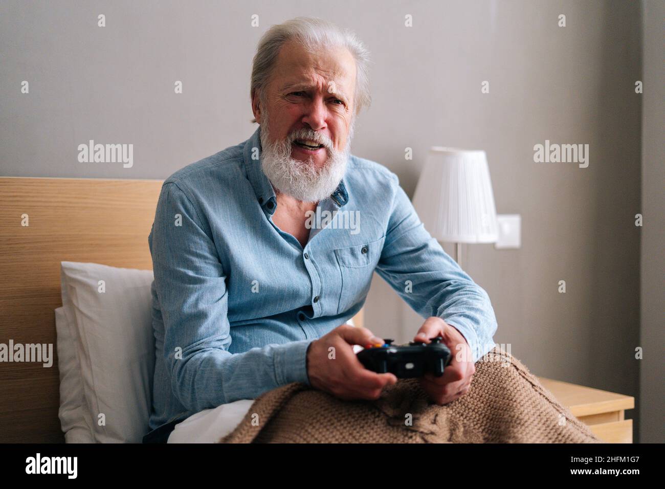 Annoyed gray-haired senior male playing online video game using gamepad ...