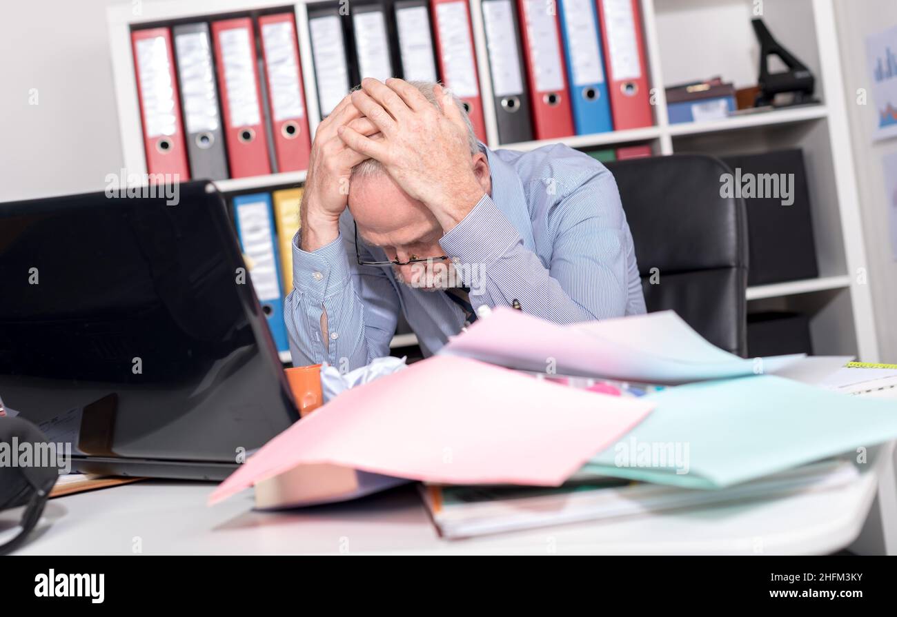Overworked businessman sitting at a messy desk in office Stock Photo ...
