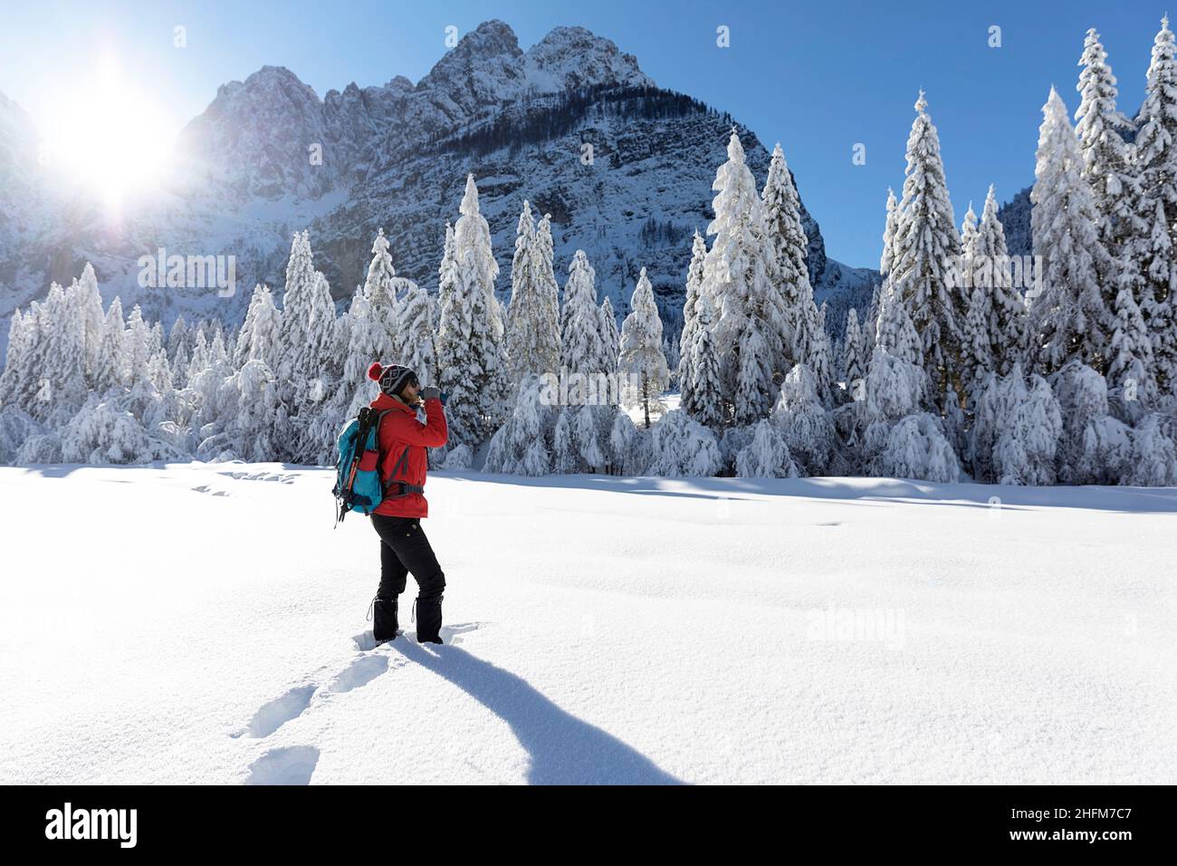 Woman in red winter jacket drinking tea from thermos while hiking in ...
