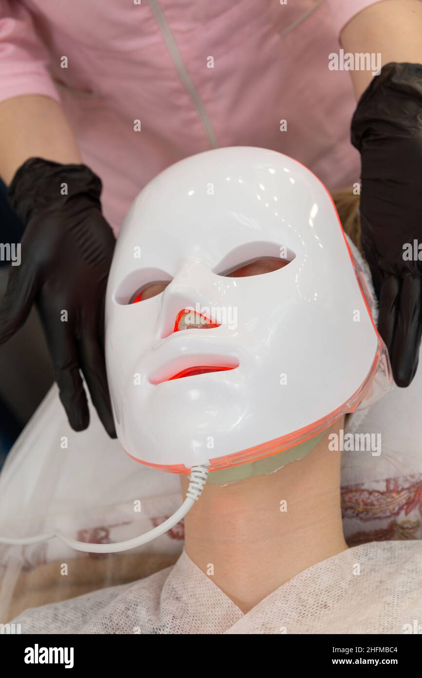 Woman lies in bed with led light therapy facial mask and relax. Led ...