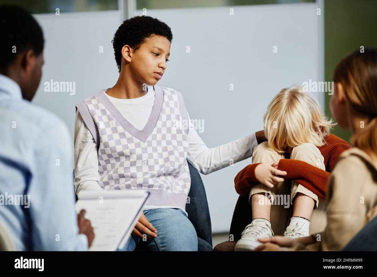 Portrait of teenage girl comforting little boy crying in group therapy ...