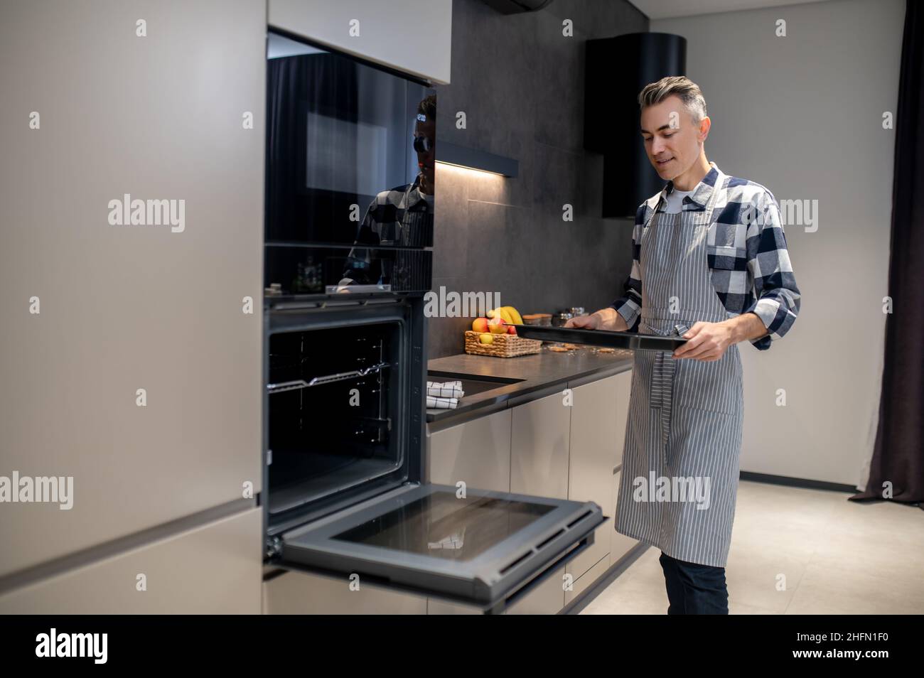 Man with baking sheet standing near open oven Stock Photo - Alamy