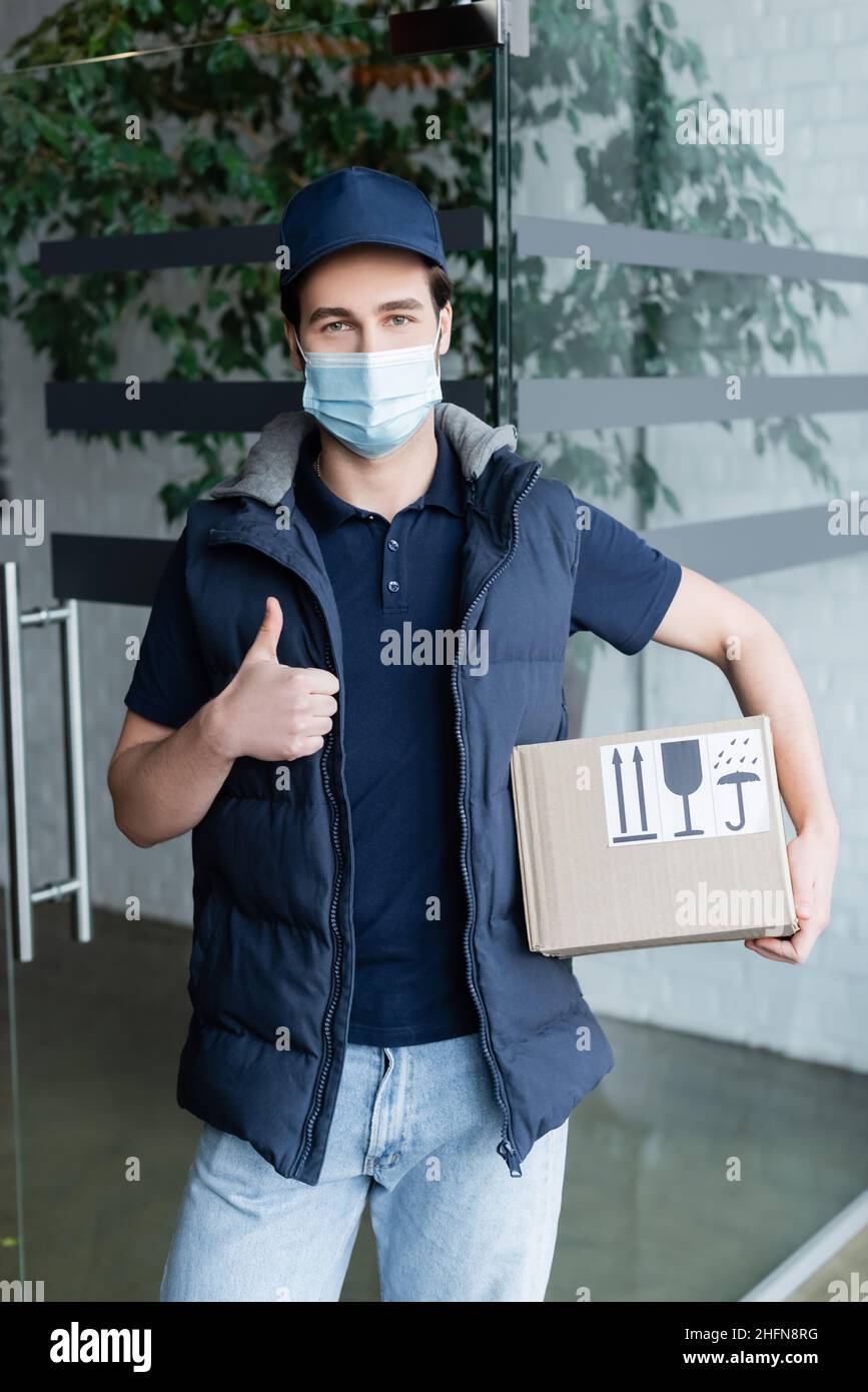 Courier in medical mask holding box with symbols and showing like in ...