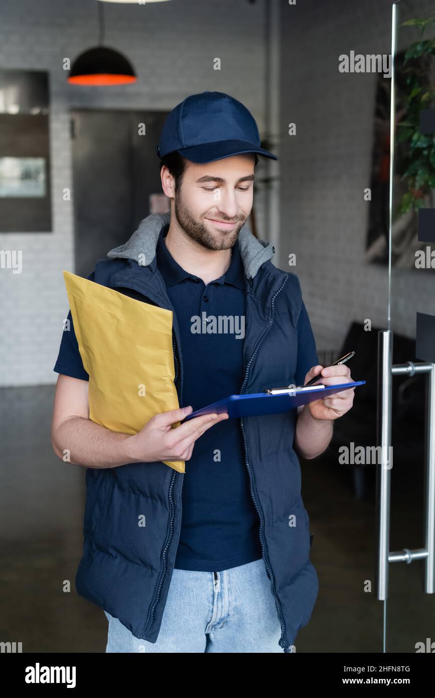 Positive delivery man holding parcel and writing on clipboard in ...
