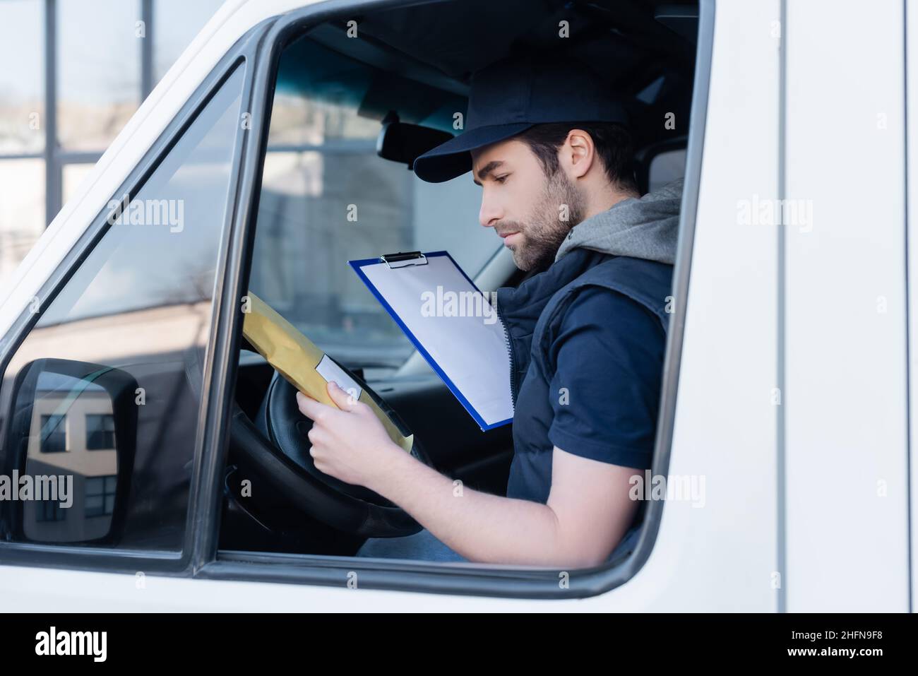 Side view of courier holding clipboard and parcel in car Stock Photo ...