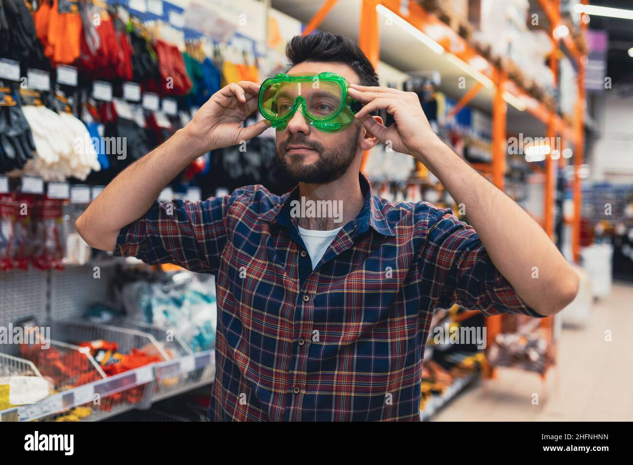 a man in a hardware store chooses safety goggles for construction work ...