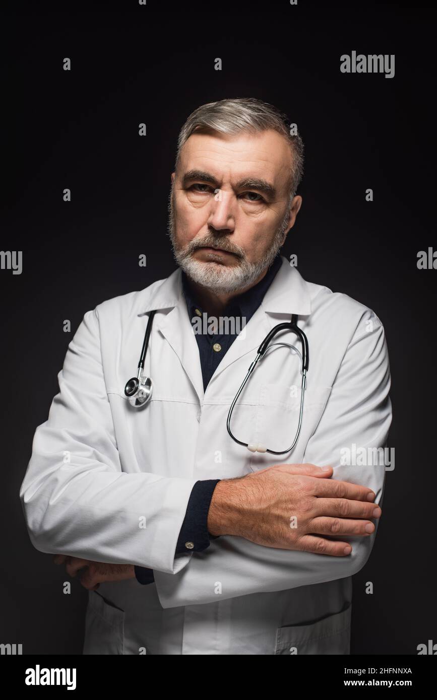 senior bearded doctor with stethoscope on neck standing with crossed ...