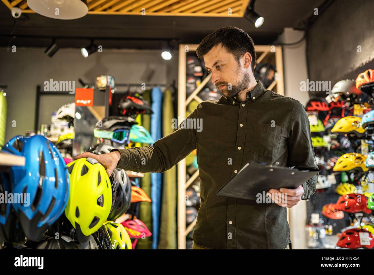 A male bike shop manager makes an inventory of sports helmets in a bike ...