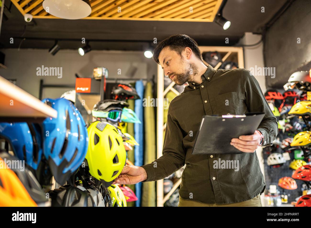 A male bike shop manager makes an inventory of sports helmets in a bike ...