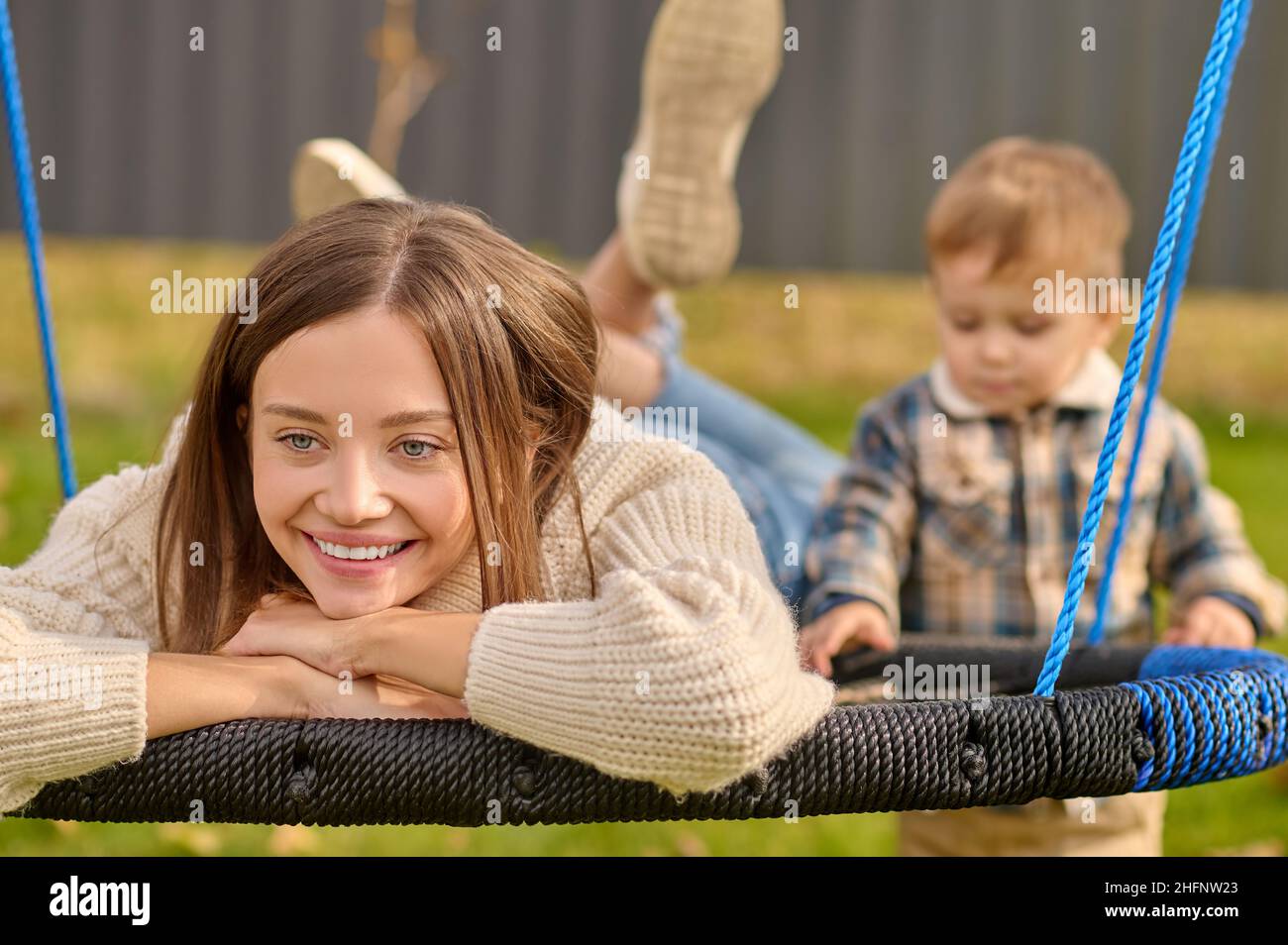 Young woman lying on swing and standing child Stock Photo - Alamy