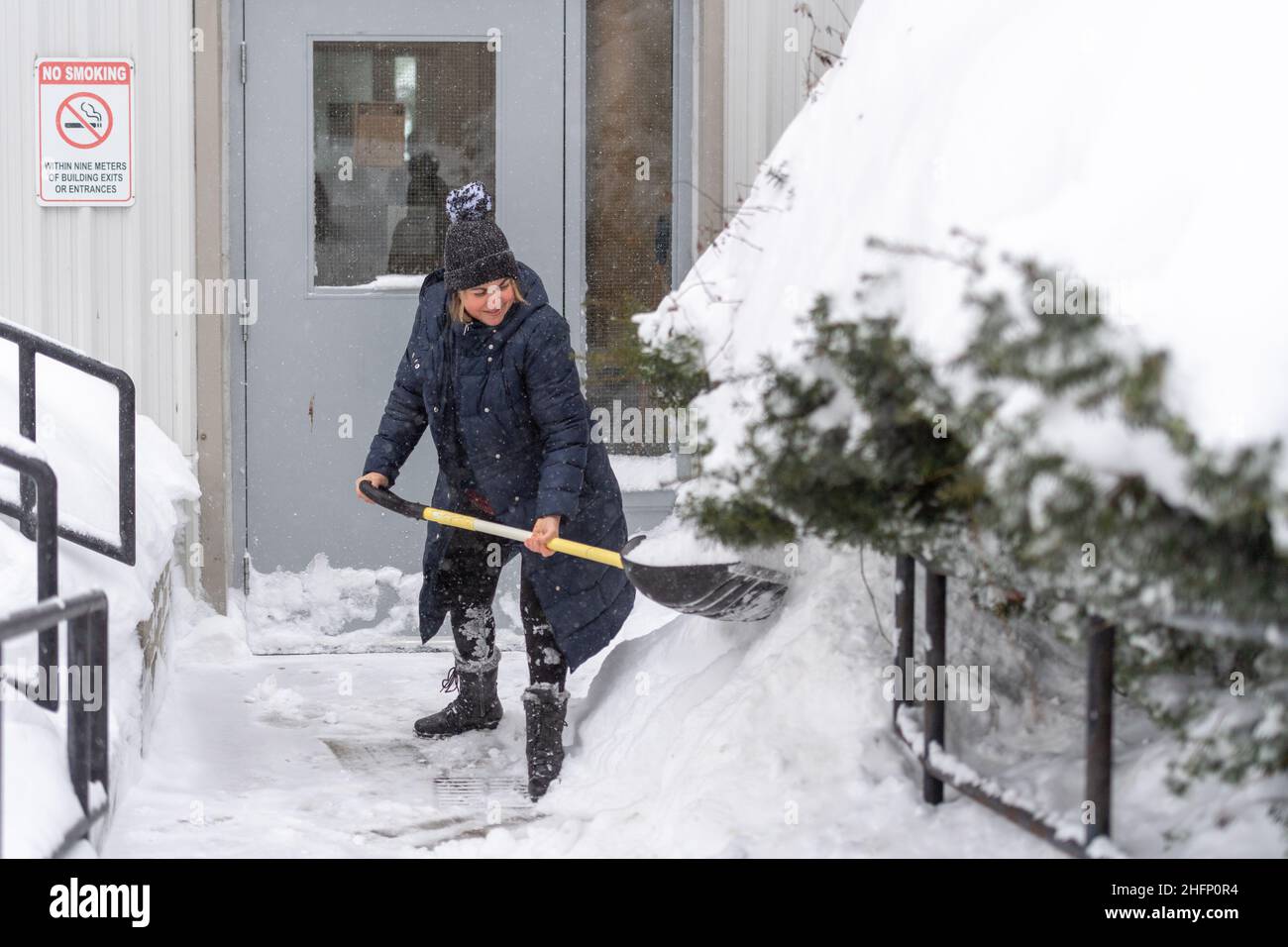A Latin American woman shovels snow at the entrance of an apartment ...