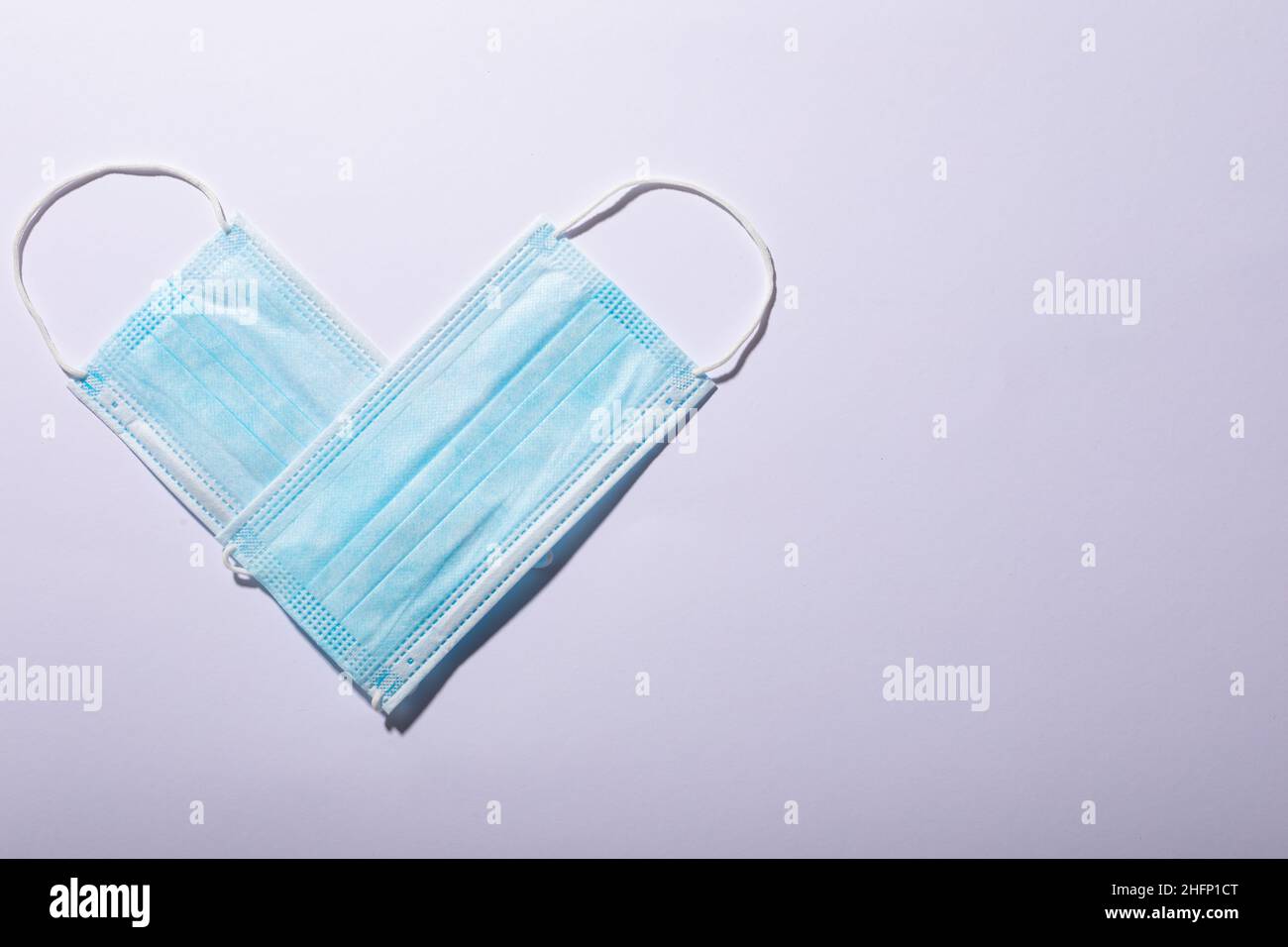 Overhead view of blue surgical masks arranged as heart shape on white ...