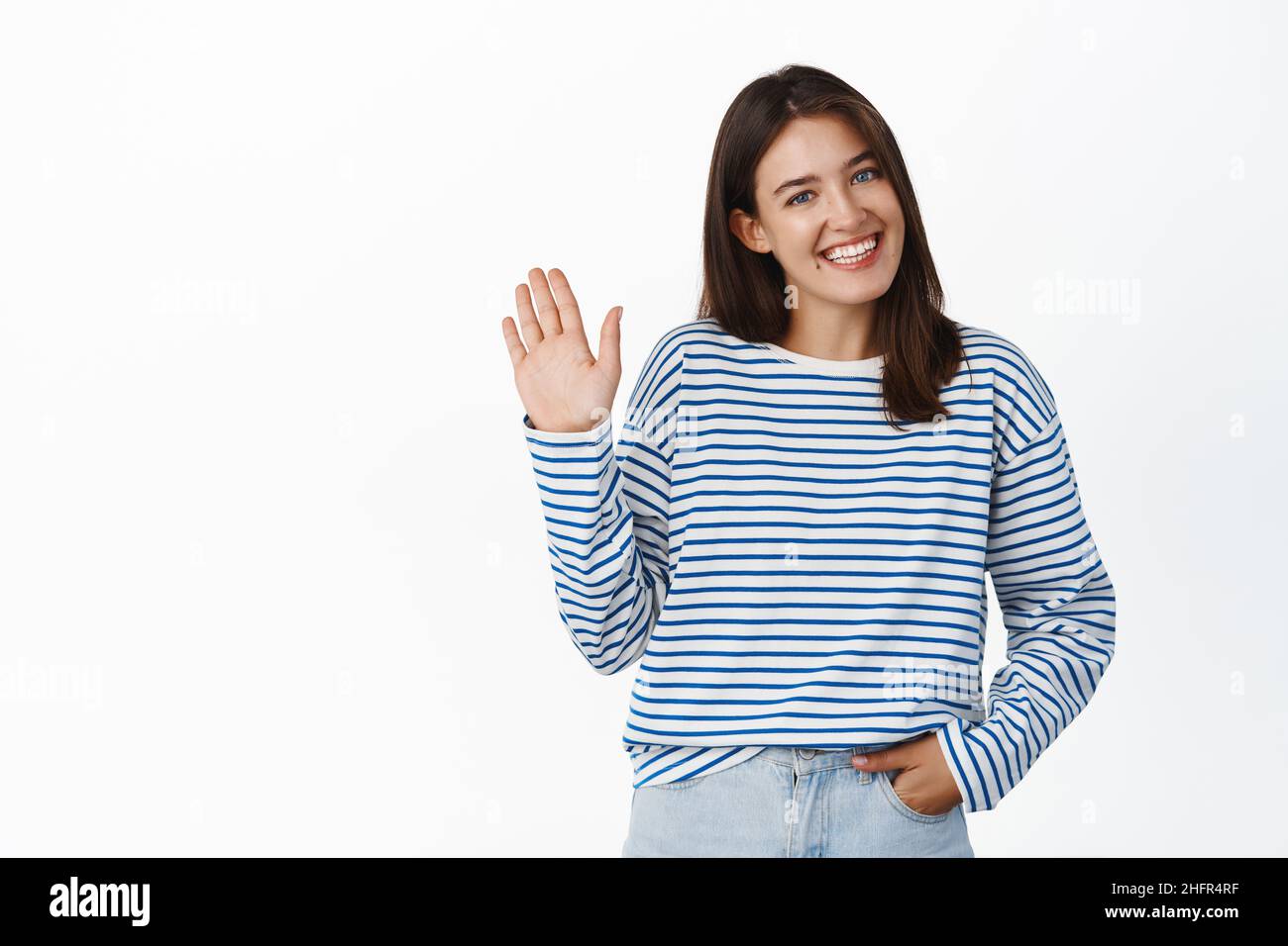 Portrait of cute happy student girl, waving hand and smiling, greeting ...