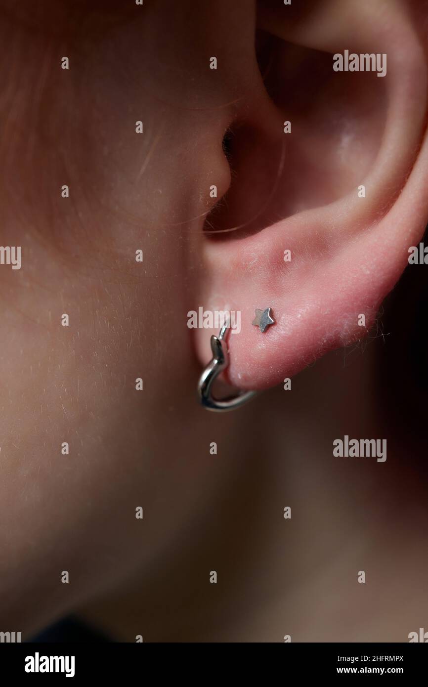 A beautician makes a puncture of the earlobe with a disposable device ...