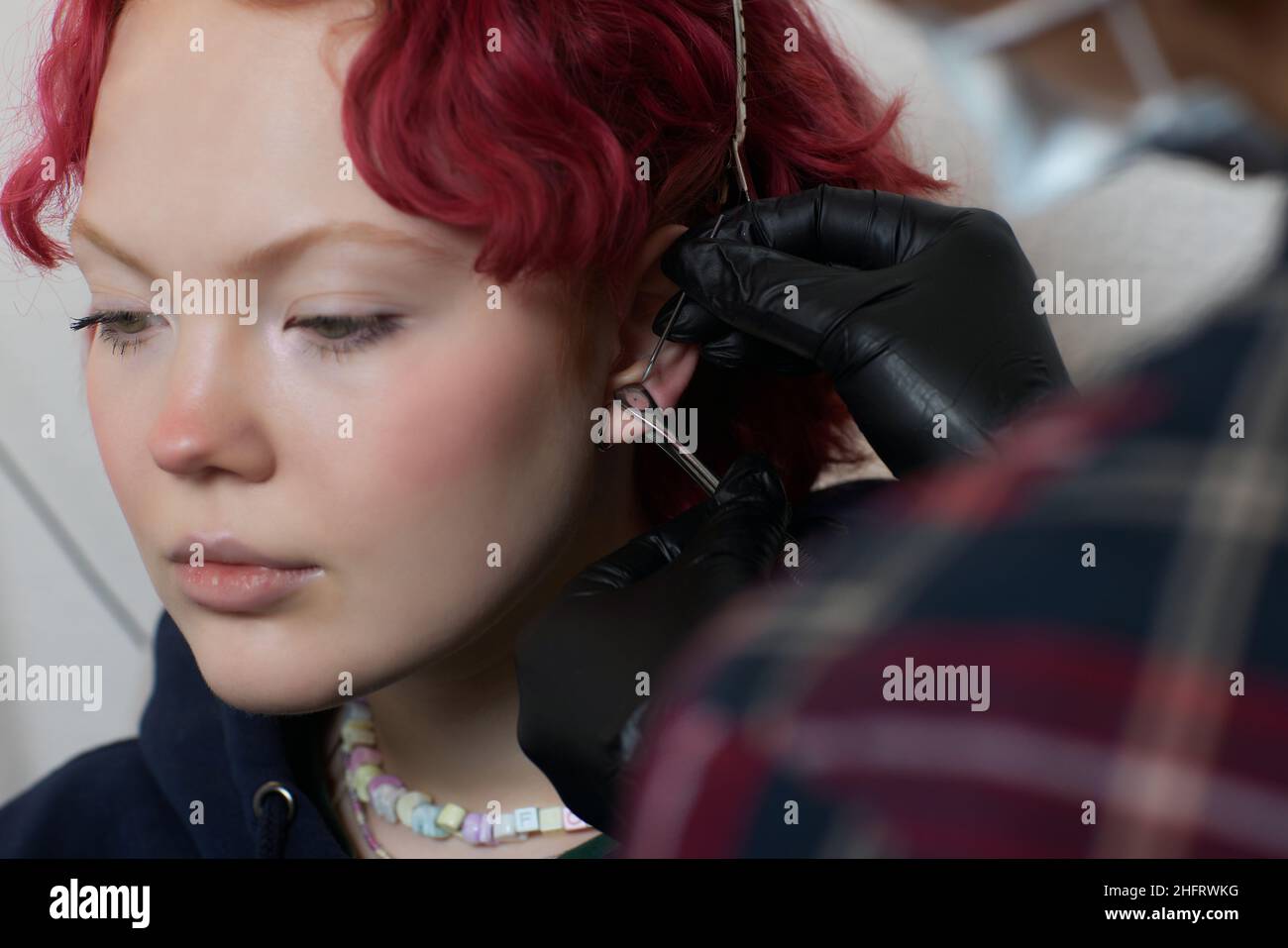 A beautician makes a puncture of the earlobe with a disposable device ...