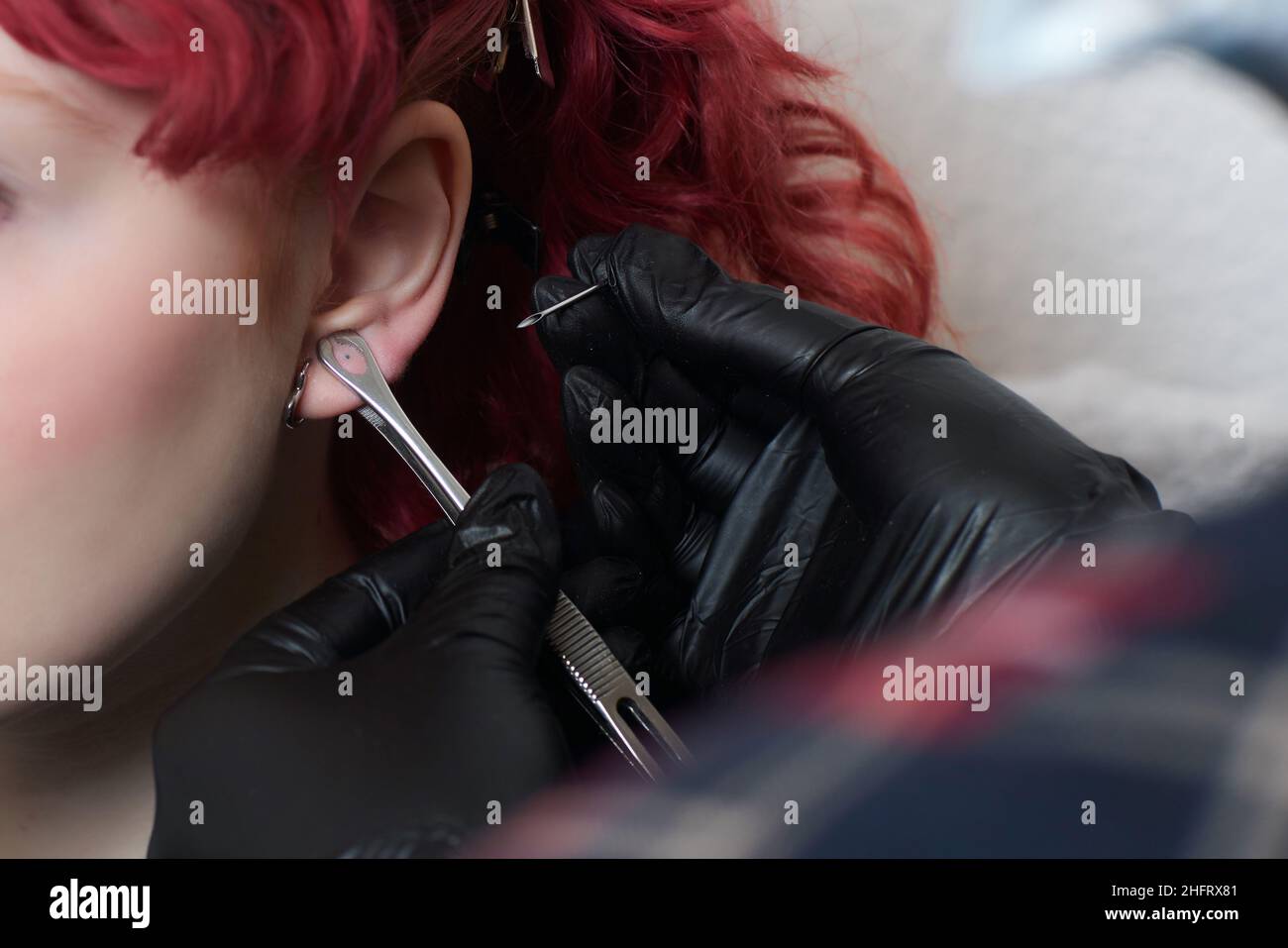 A beautician makes a puncture of the earlobe with a disposable device ...