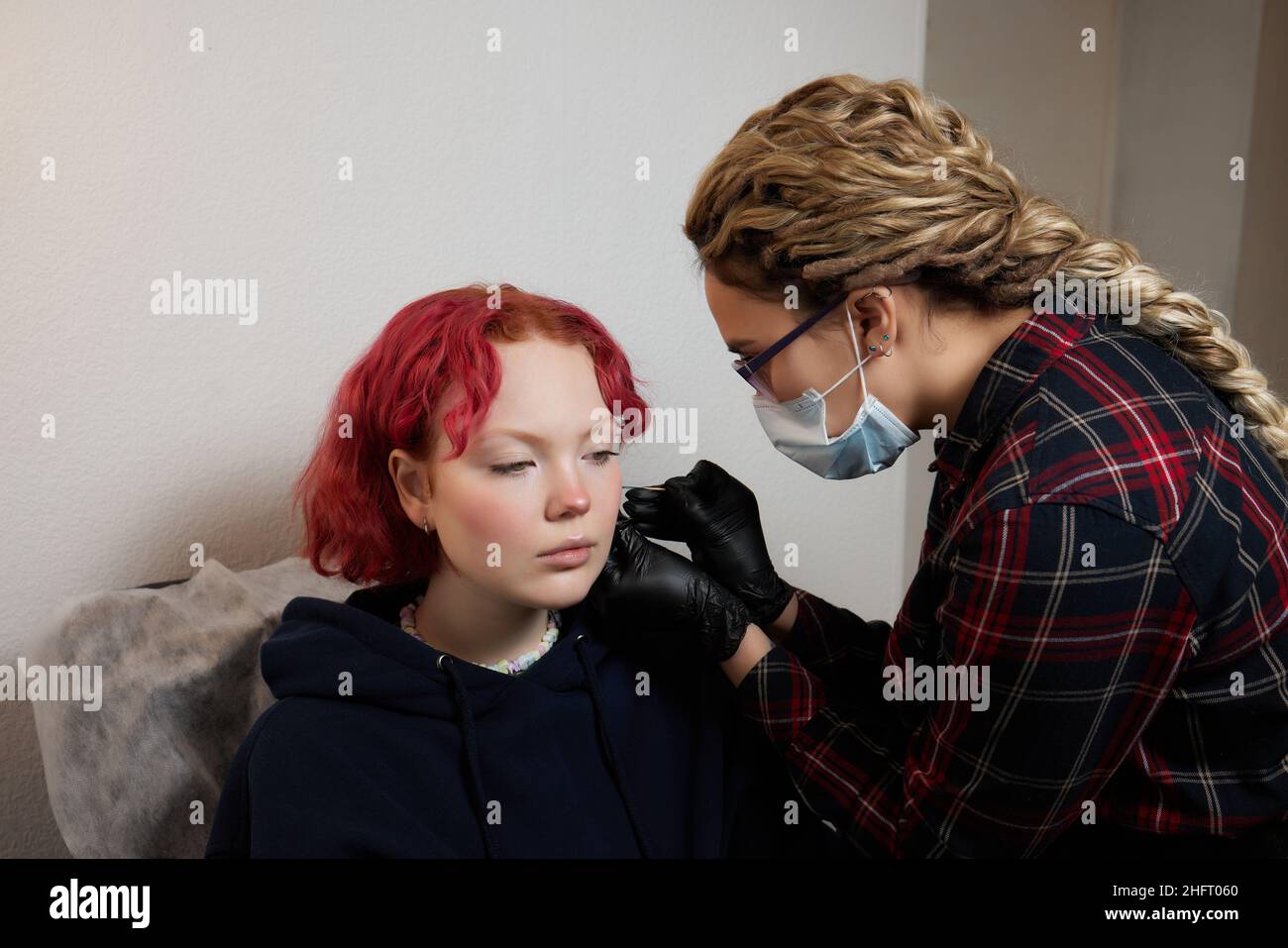 A beautician makes a puncture of the earlobe with a disposable device ...