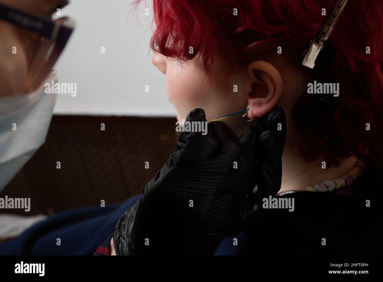 A beautician makes a puncture of the earlobe with a disposable device ...