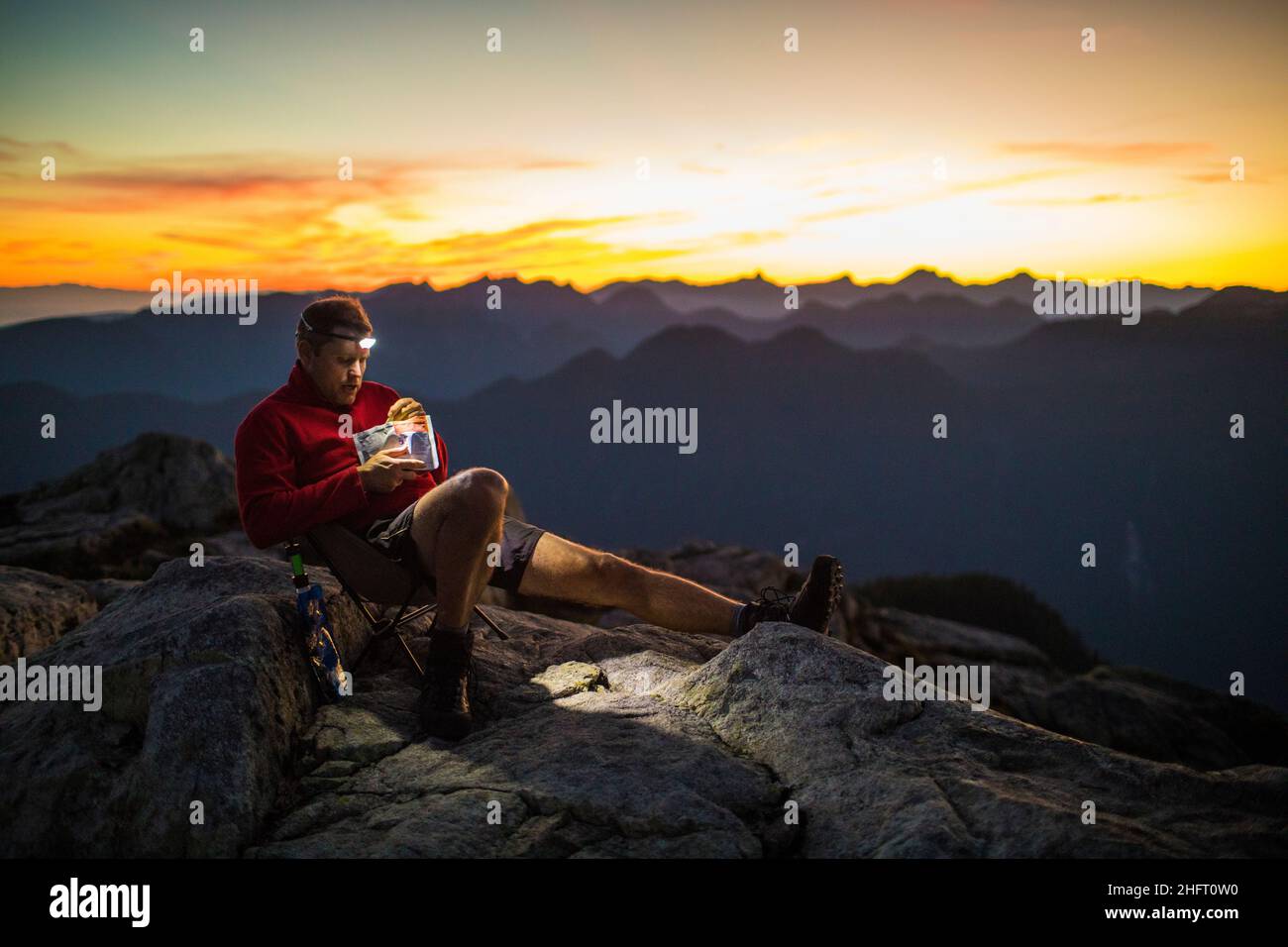 Mountain climber sitting on summit eating meal, using headlamp Stock ...