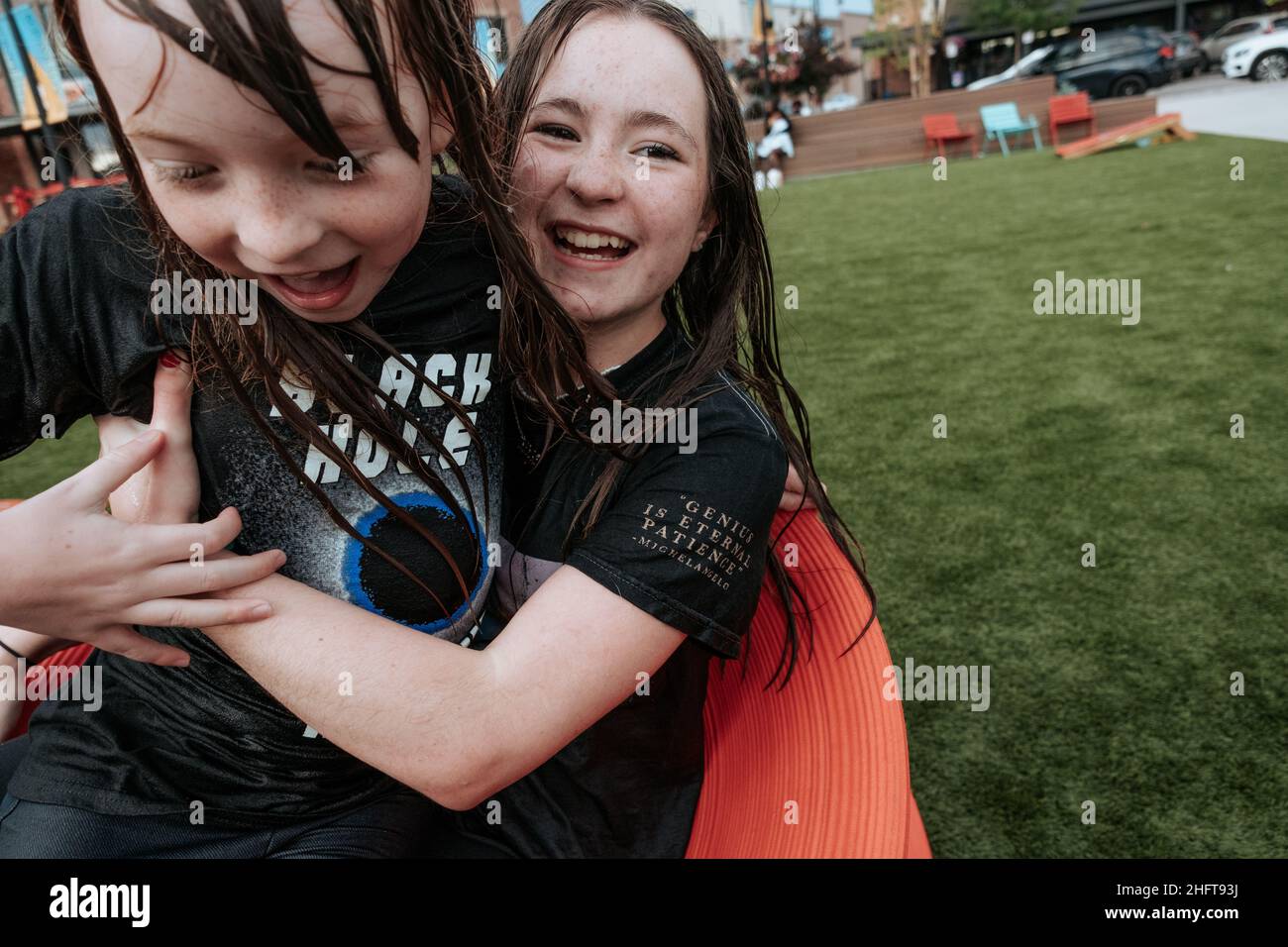 Two girls playing together on chair outside Stock Photo - Alamy