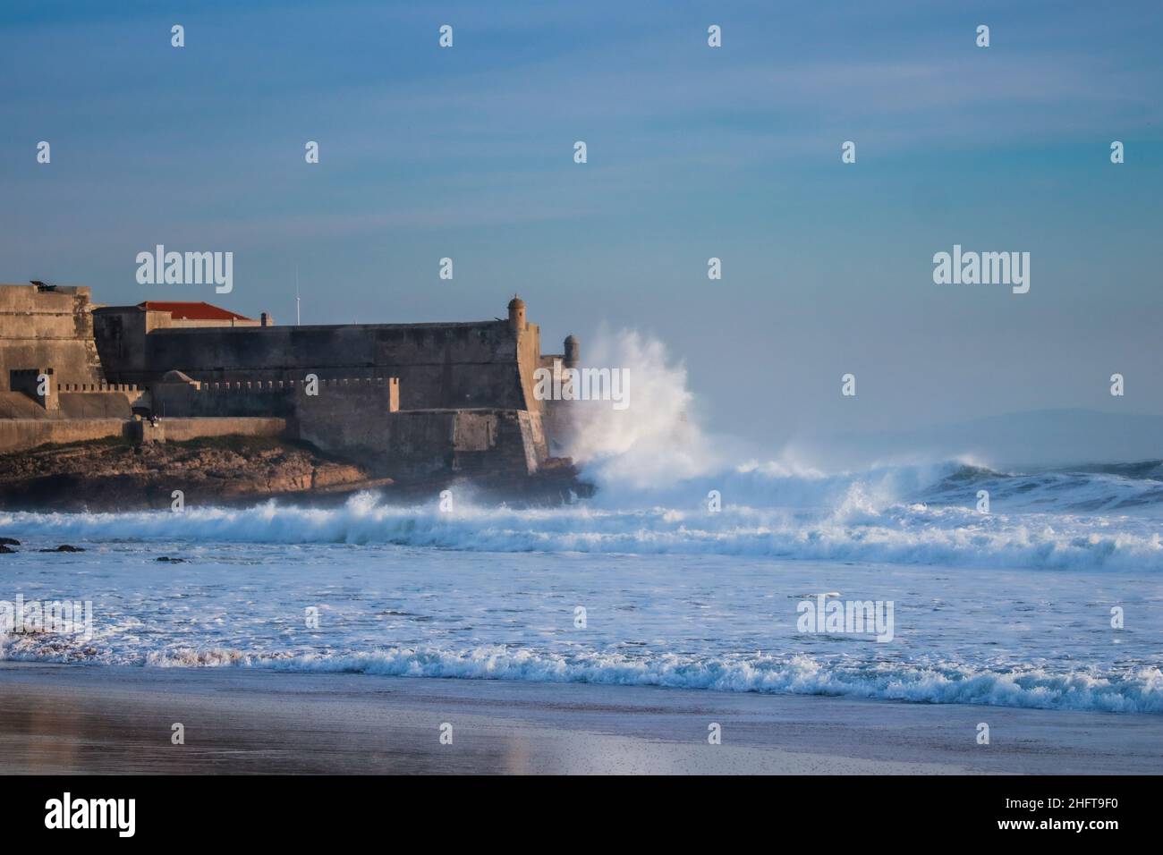 Large waves crash into a fortress near a beach. Carcavelos beach in ...