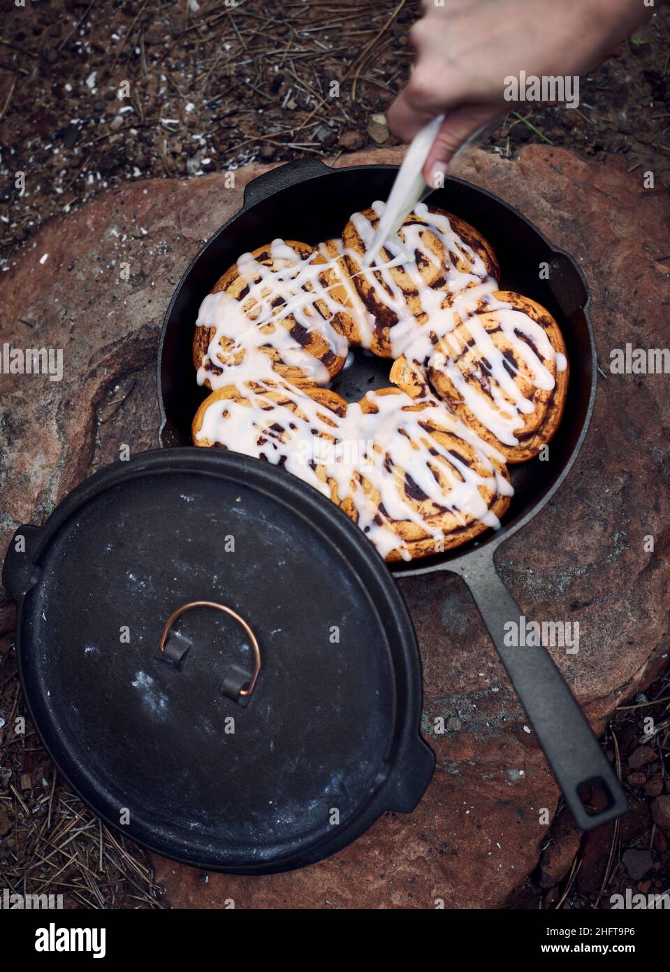 Hand pouring icing over cast iron made cinnamon rolls on a boulder ...
