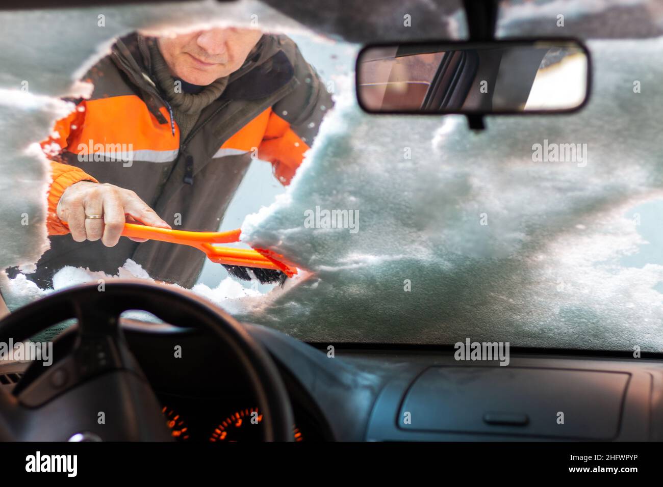 Man cleaning car windshield with scraper and brush from snow and ice ...