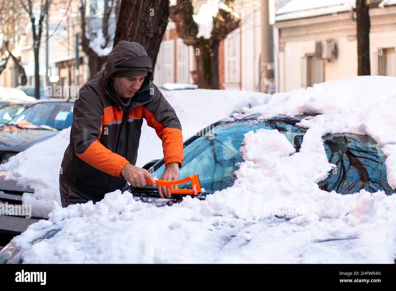 A man cleaning car windshield with scraper and brush from snow and ice ...