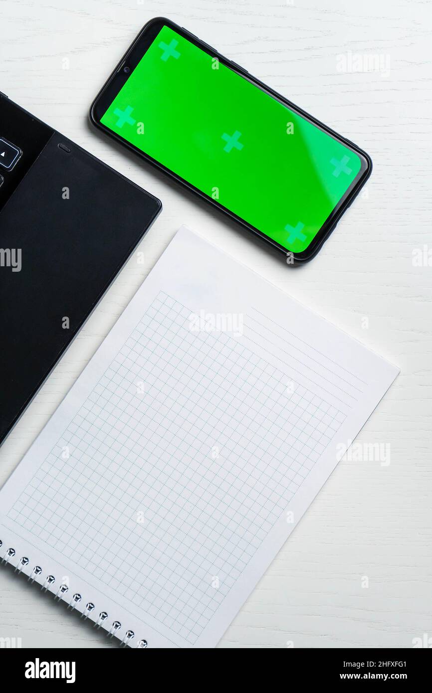 White notepad laptop and green screen smartphone on white tables, copy ...