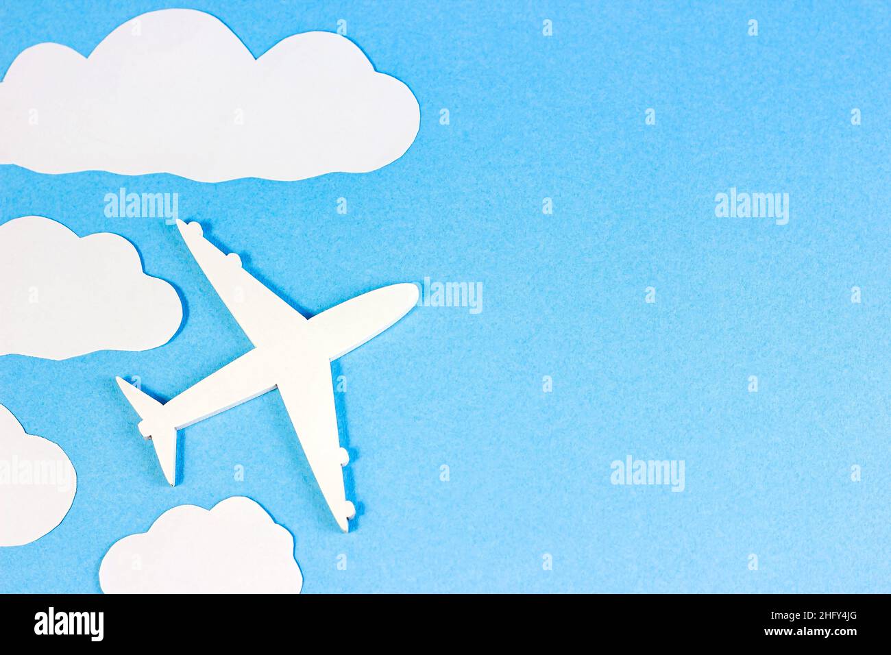 White plane model on light sky blue background with paper clouds and ...
