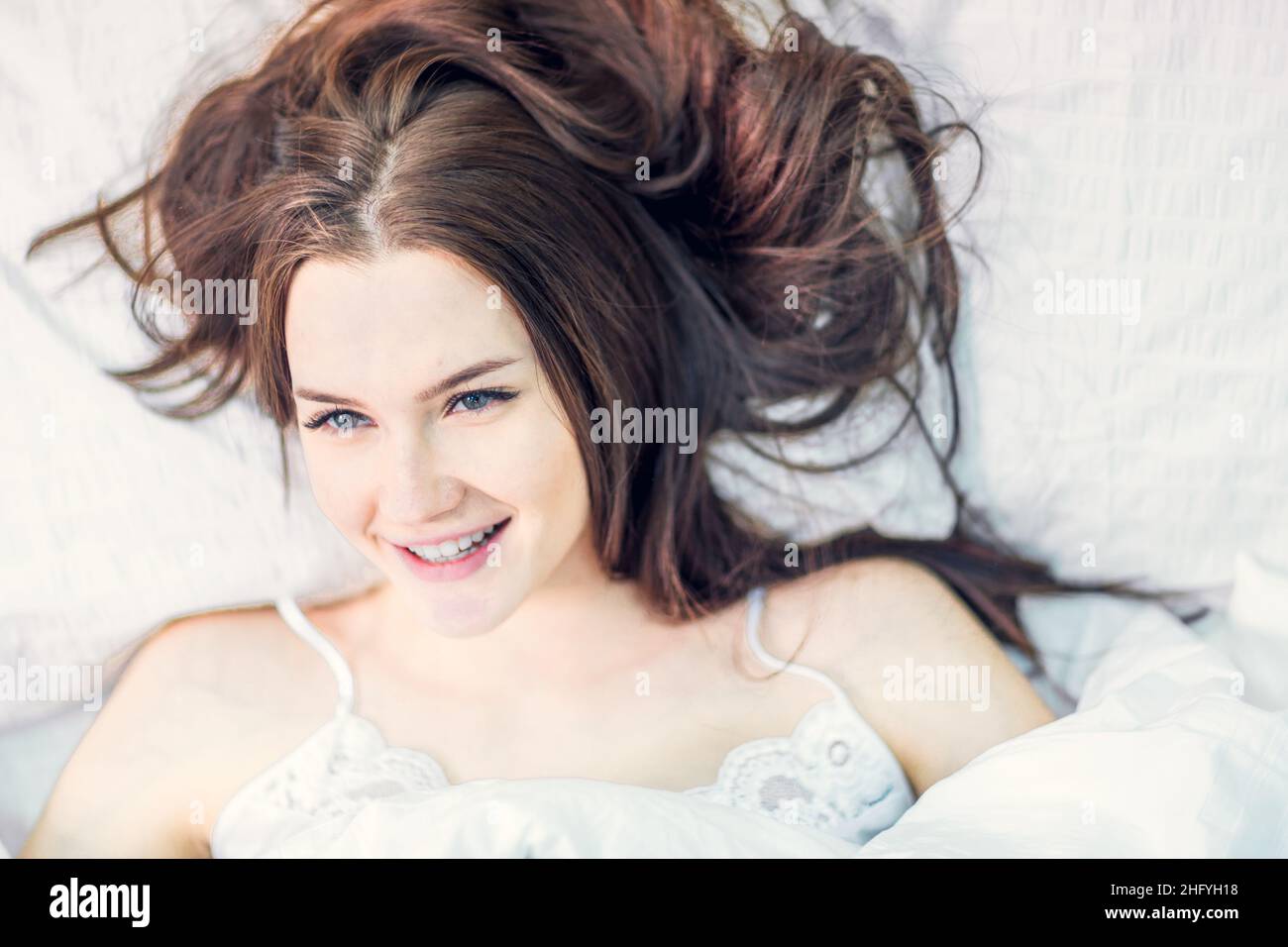 Portrait of a beautiful happy young girl on the bed in a white bed ...