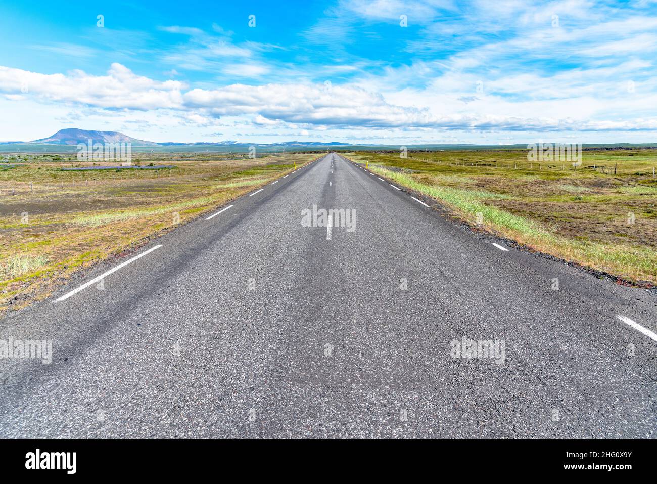 Deserted straight stretch of a road running through meadows in Iceland ...