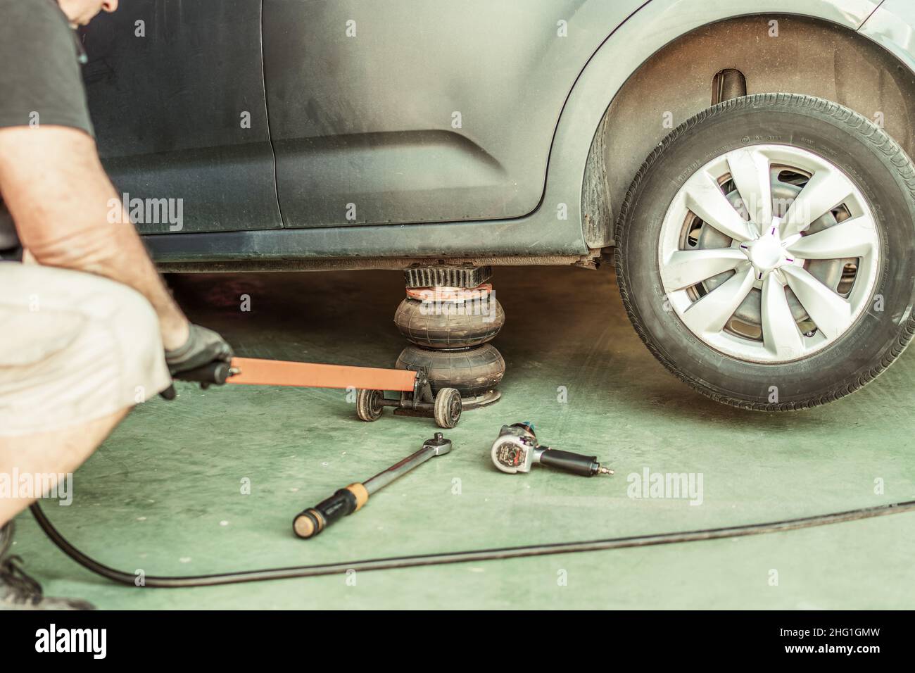 Mechanic using a pneumatic jack under a car to lift it into a garage ...
