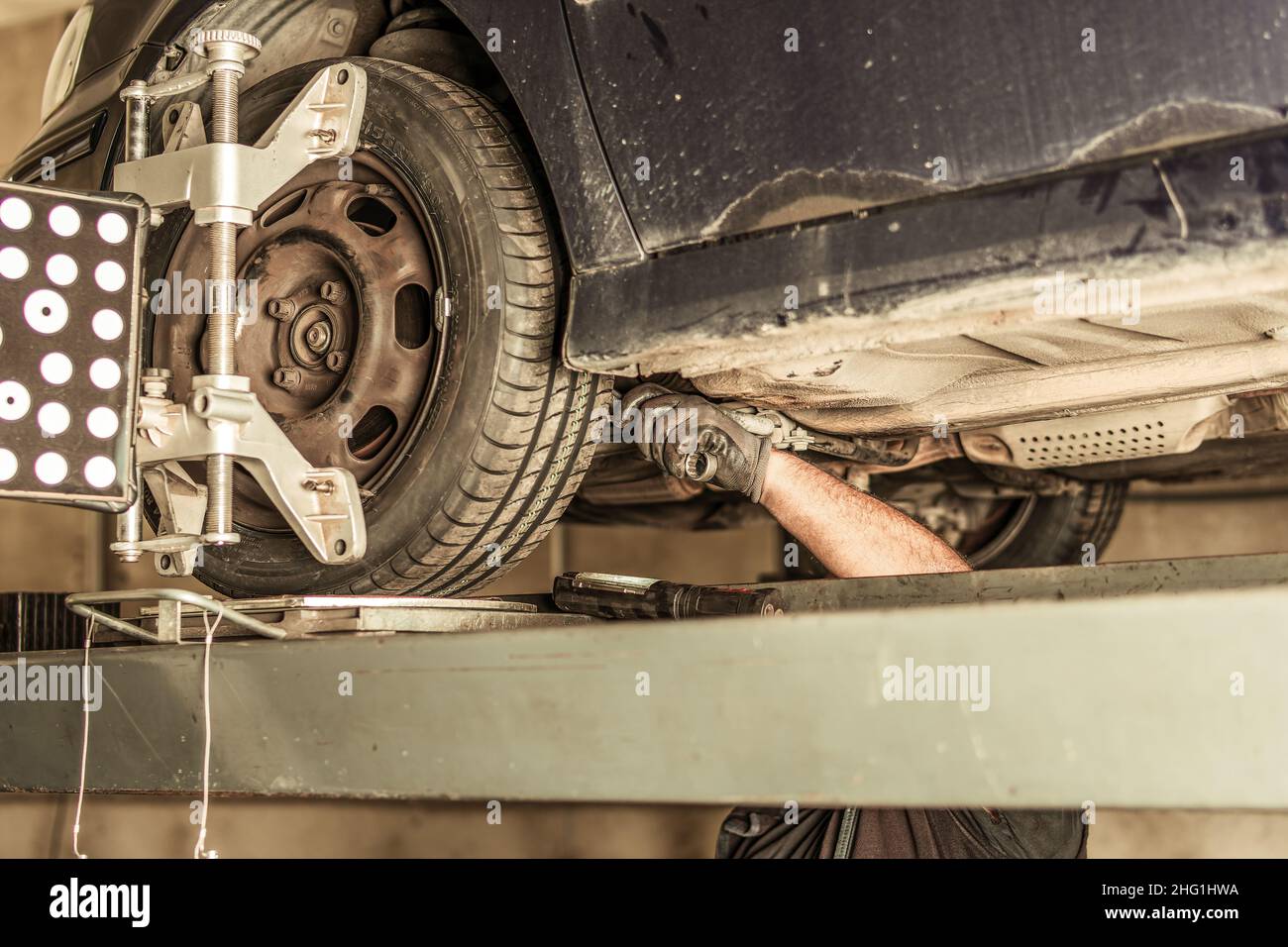 Mechanic aligning the steering of a car lifted by a jack in a garage ...